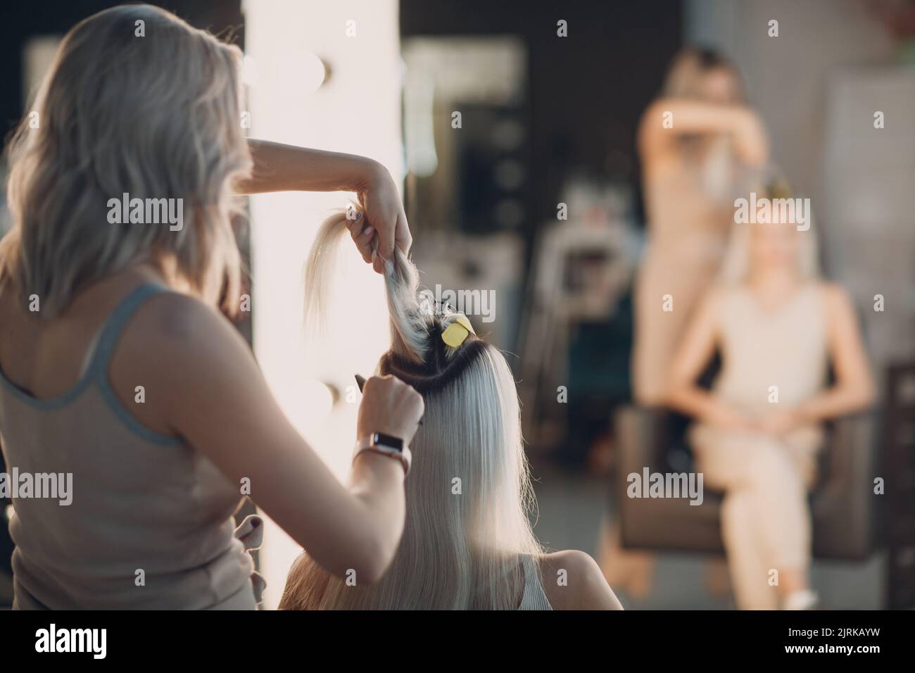 Hairdresser female making hair extensions to young woman with blonde ...