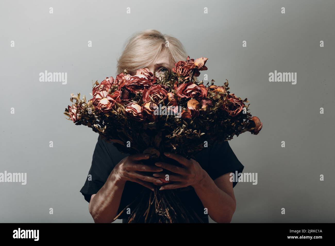 Upset elderly woman hold withered dry old rose flowers bouquet. Old age ...
