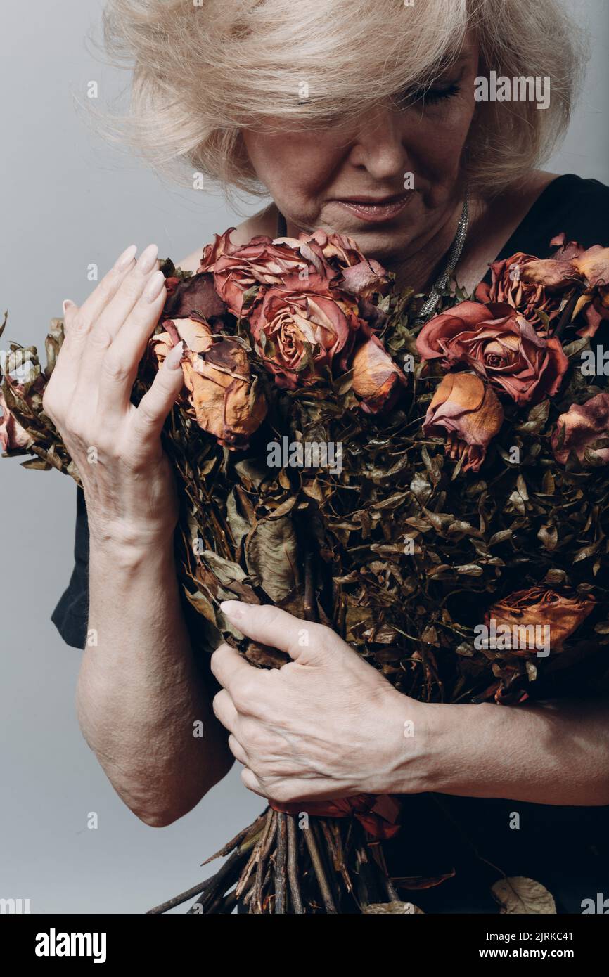 Upset elderly woman hold withered dry old rose flowers bouquet. Old age ...
