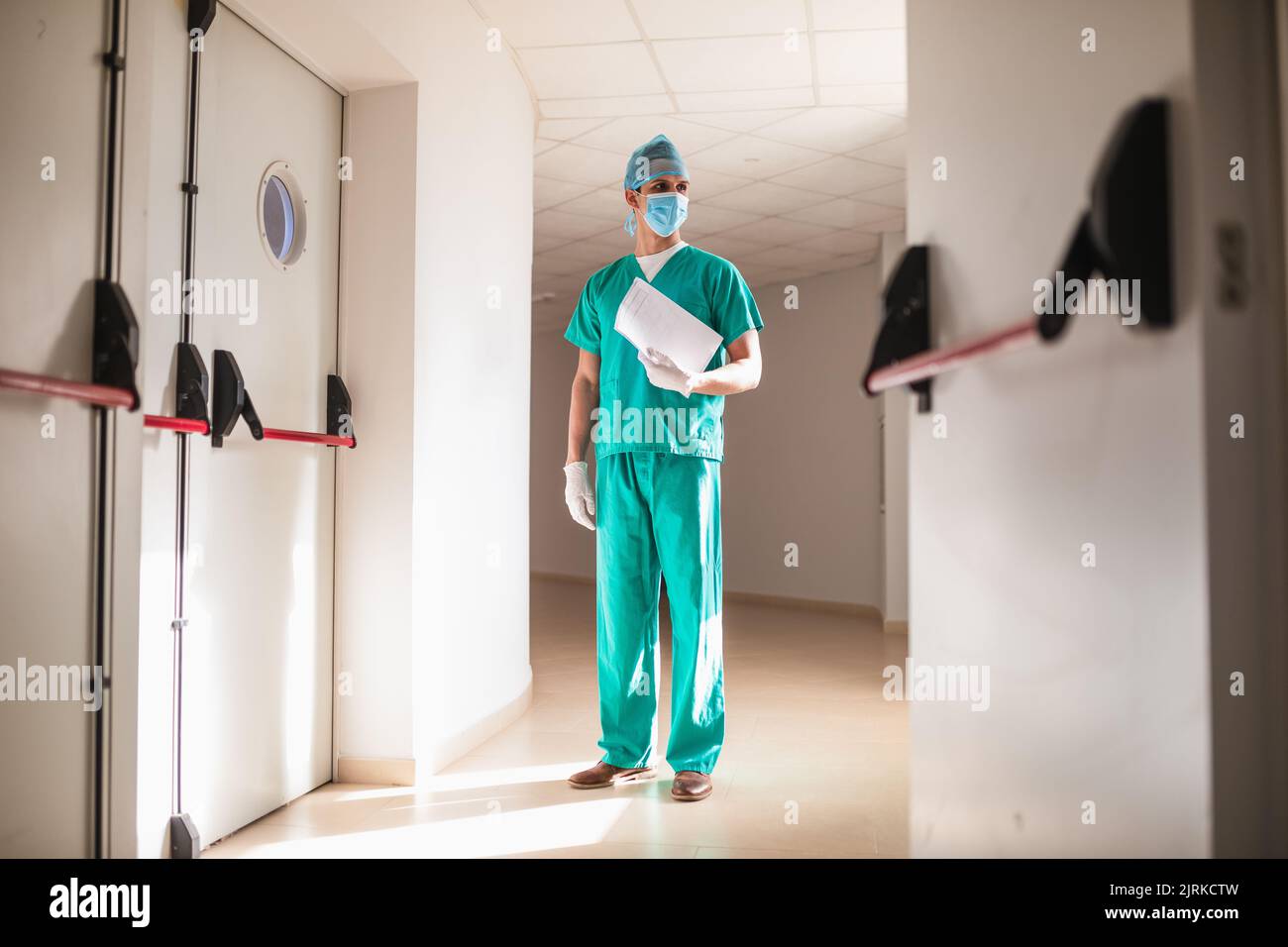 Male medic in sterile mask and gloves standing near door with window in ...