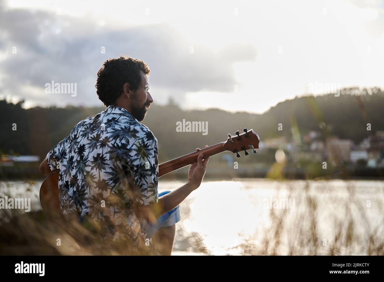 Back view of male musician playing acoustic guitar while sitting on ...