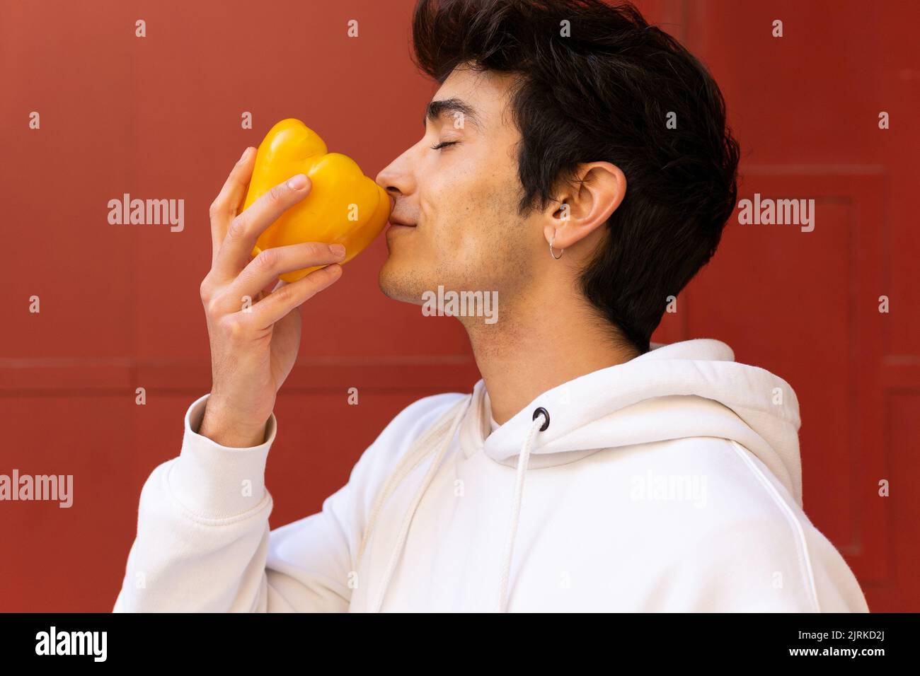Side view of content male enjoying smell of fresh red pepper while ...