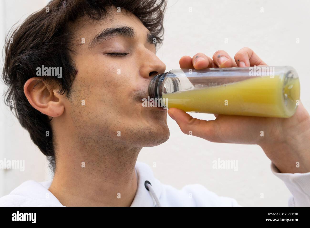 Carefree male drinking natural orange juice from bottle while enjoying taste with closed eyes ...