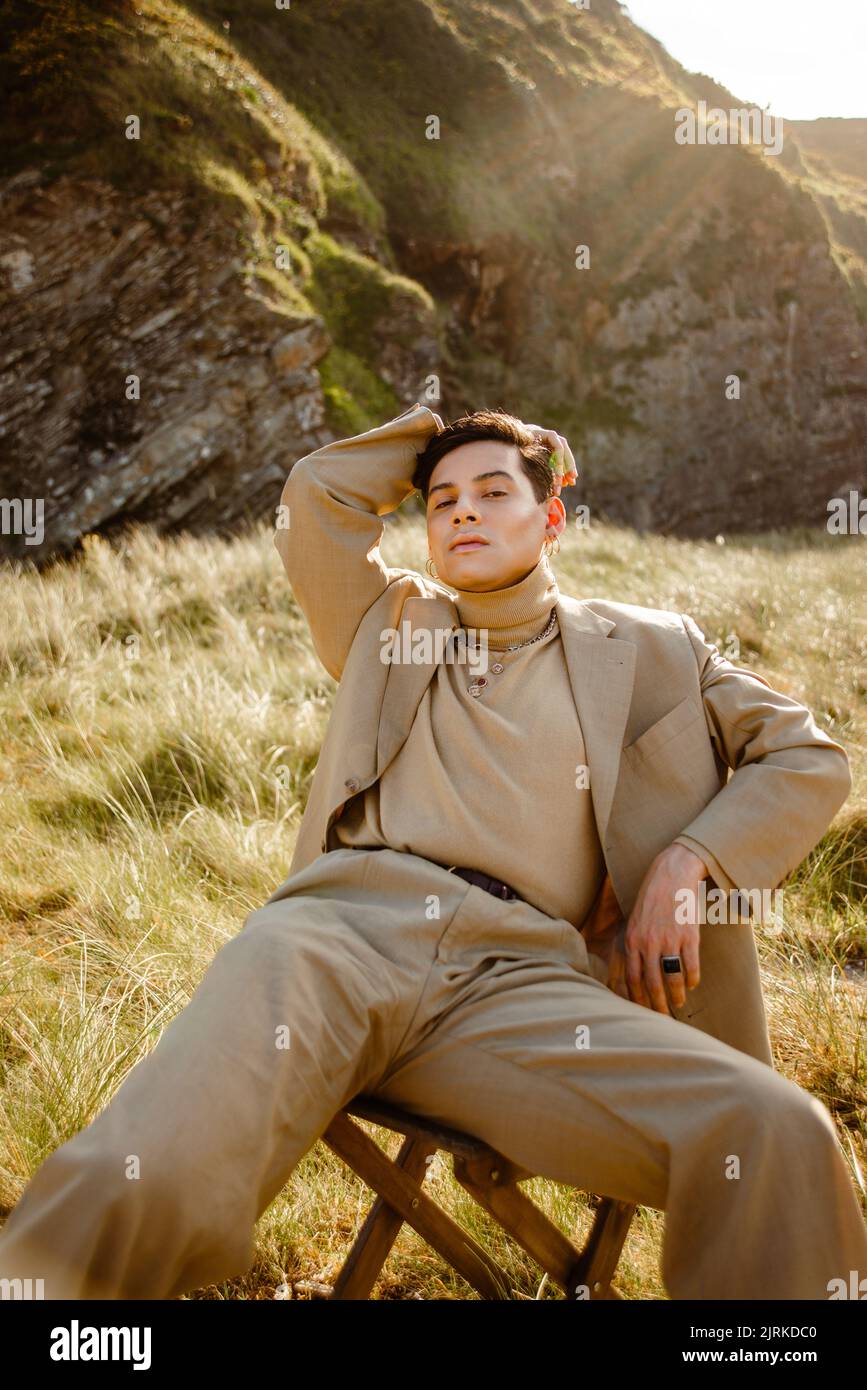 Full body male model in trendy suit sitting on chair in grassy field ...