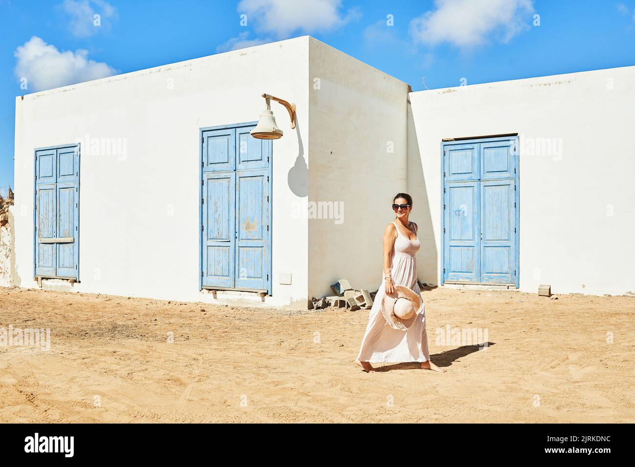 Full body barefoot happy female in maxi sundress strolling on sandy ...