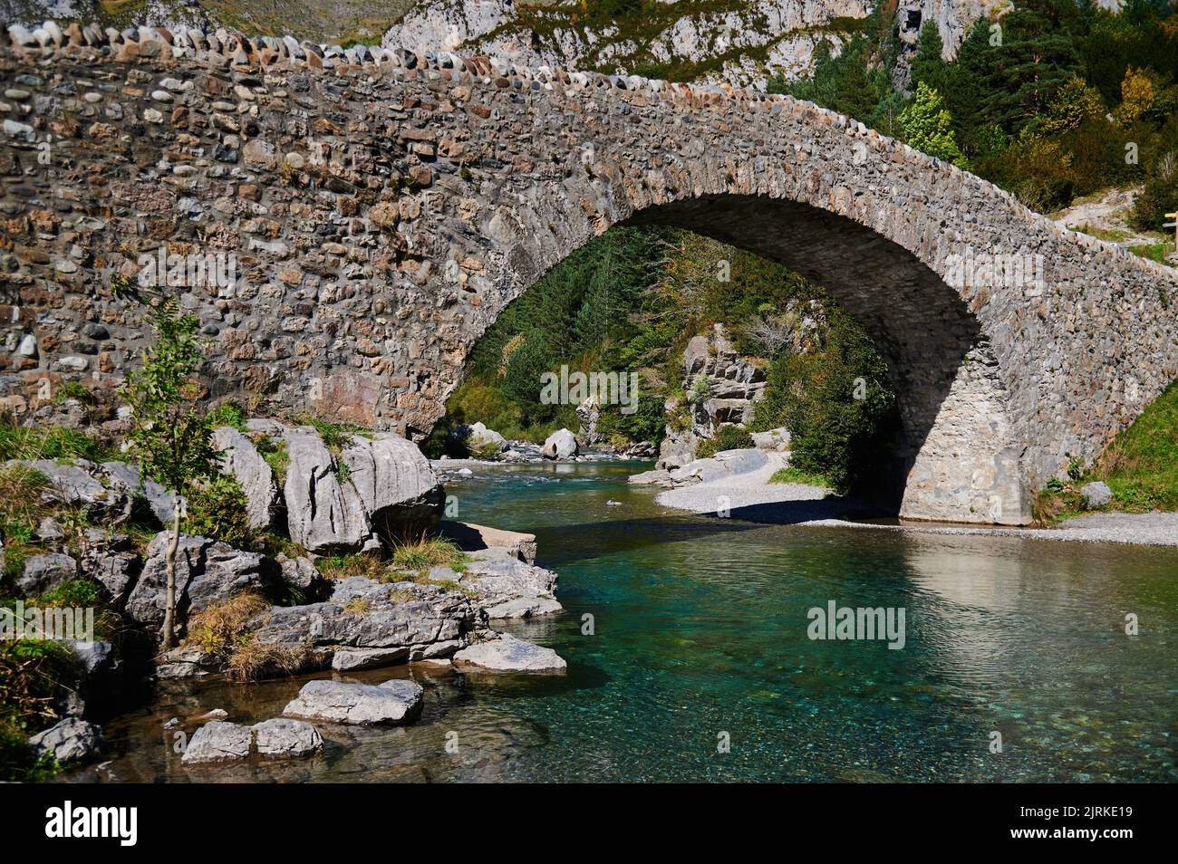 Medieval arched bridge crossing rippling river flowing among shoe with ...
