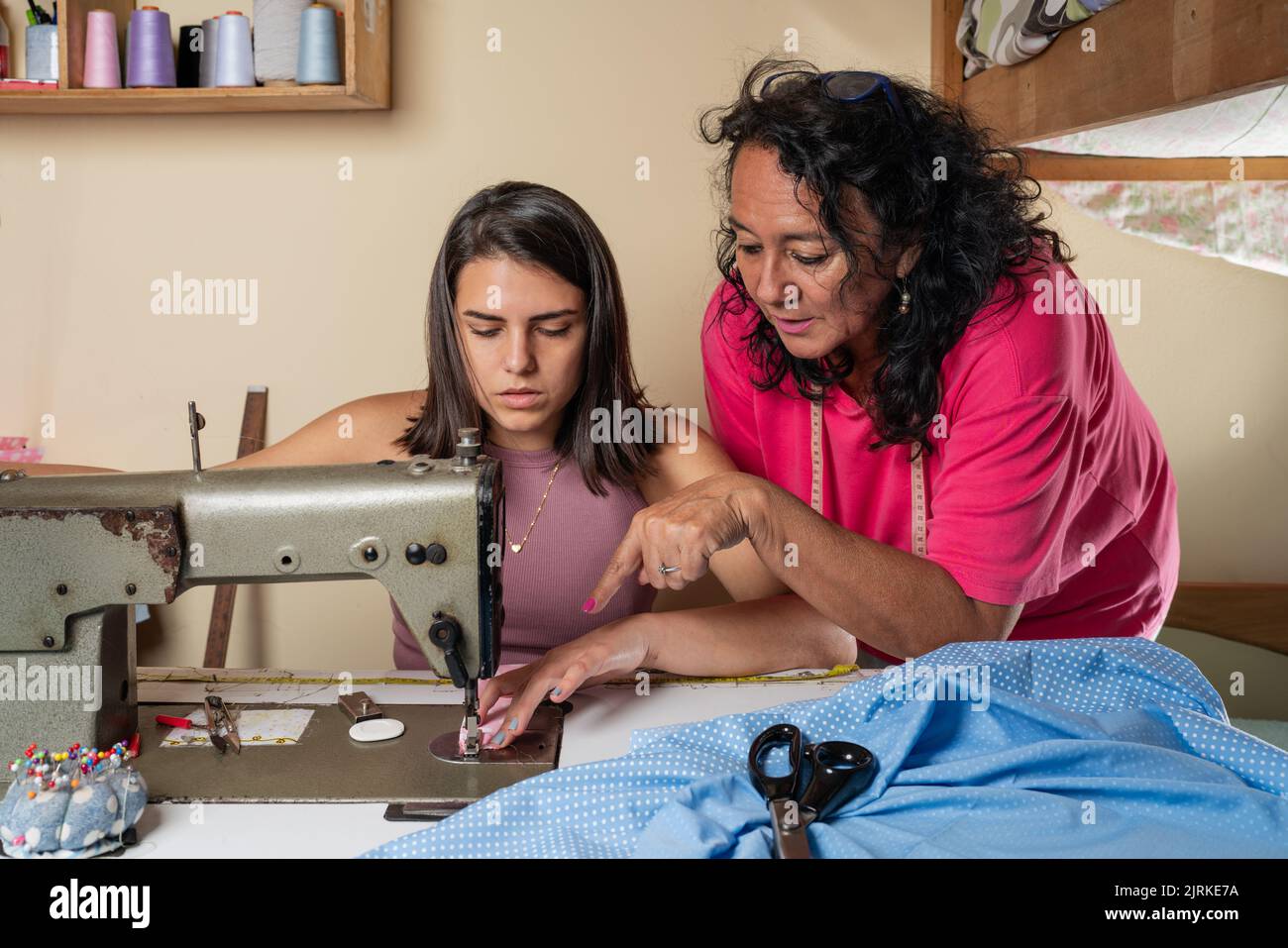 Hispanic seamstress teaching daughter sewing on professional machine at ...