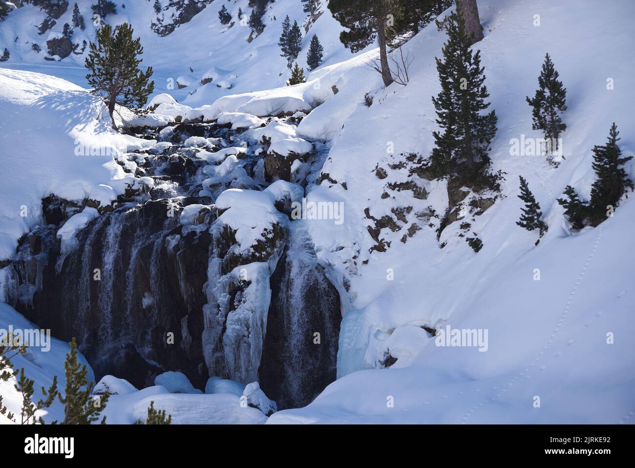 Clear frozen brook flowing on rocky formation covered with snow in ...