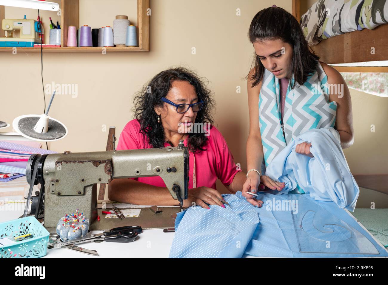 Hispanic seamstress with daughter at table with sewing machine and ...