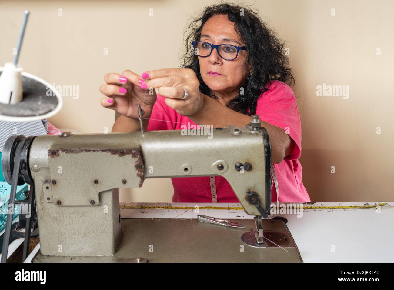 Skilled Hispanic seamstress with black hair in eyeglasses threading ...