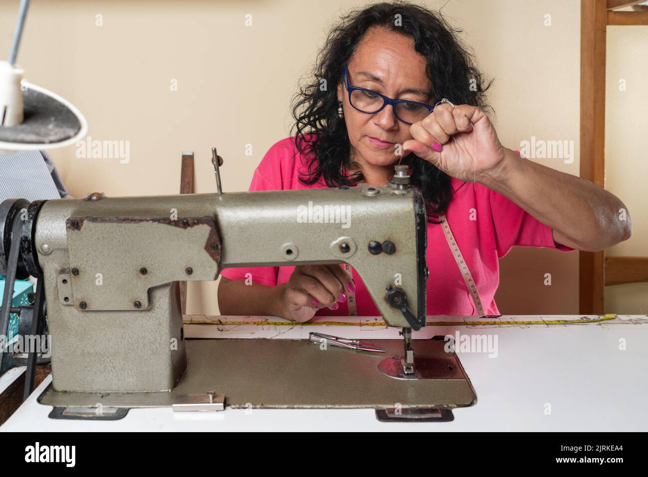 Skilled Hispanic seamstress with black hair in eyeglasses threading ...