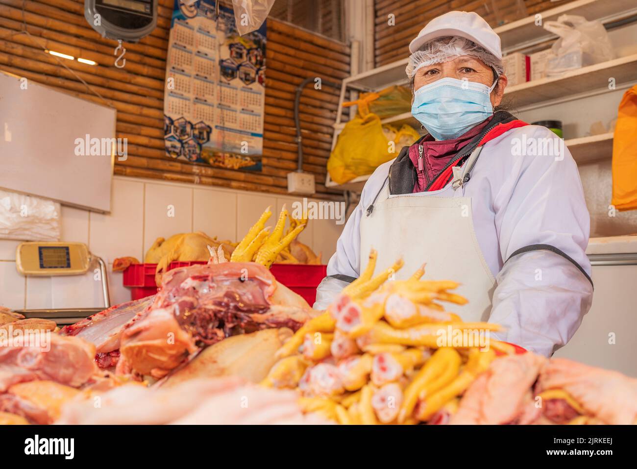 Peruvian female seller in face mask and apron standing behind counter ...