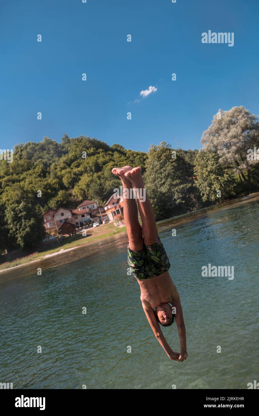 Young teen boy jumping flying and diving in the river. Clear blue sky ...