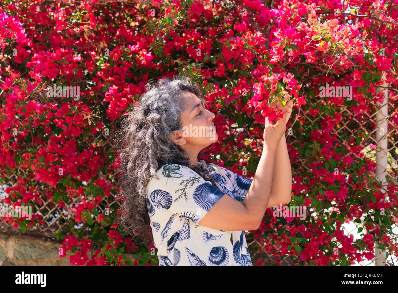 Side view of mature ethnic female with curly gray hair enjoying aroma ...