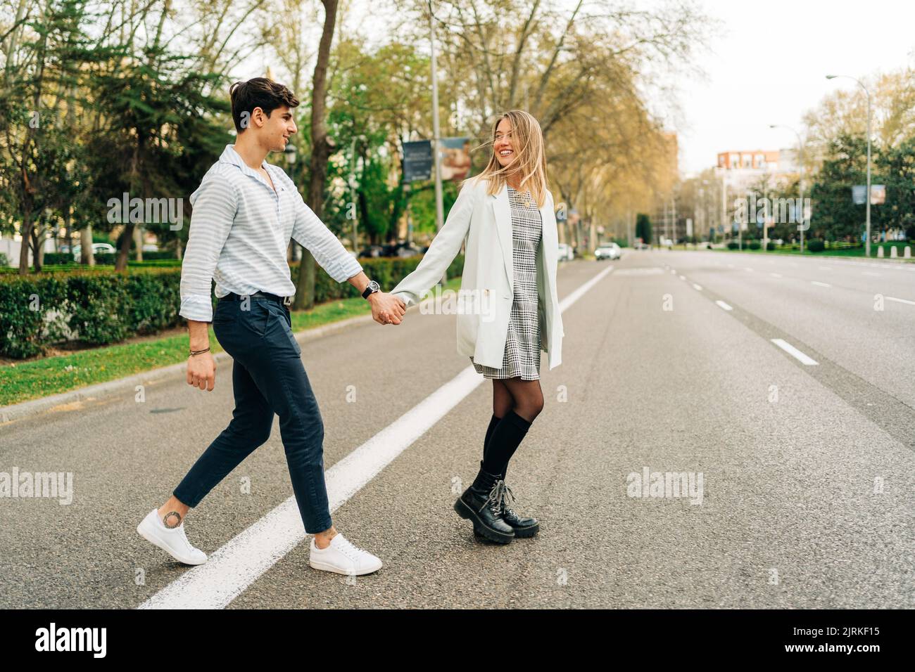 Side view of content stylish couple holding hands and crossing road ...