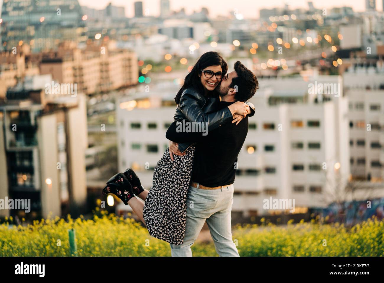 Ethnic male raising and kissing smiling female beloved while spending time together against ...