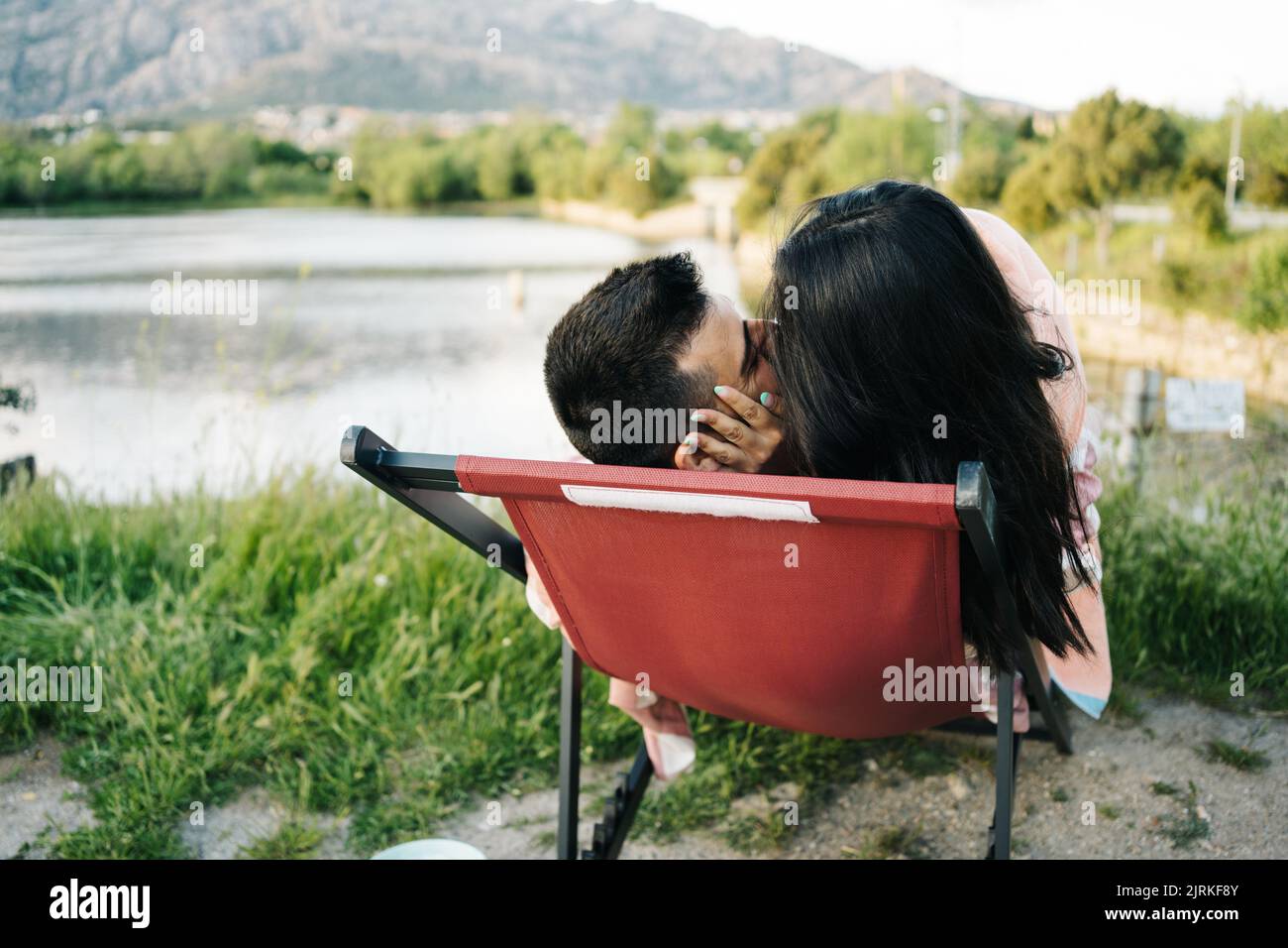 Loving couple of travelers relaxing in camping chair and kissing during ...