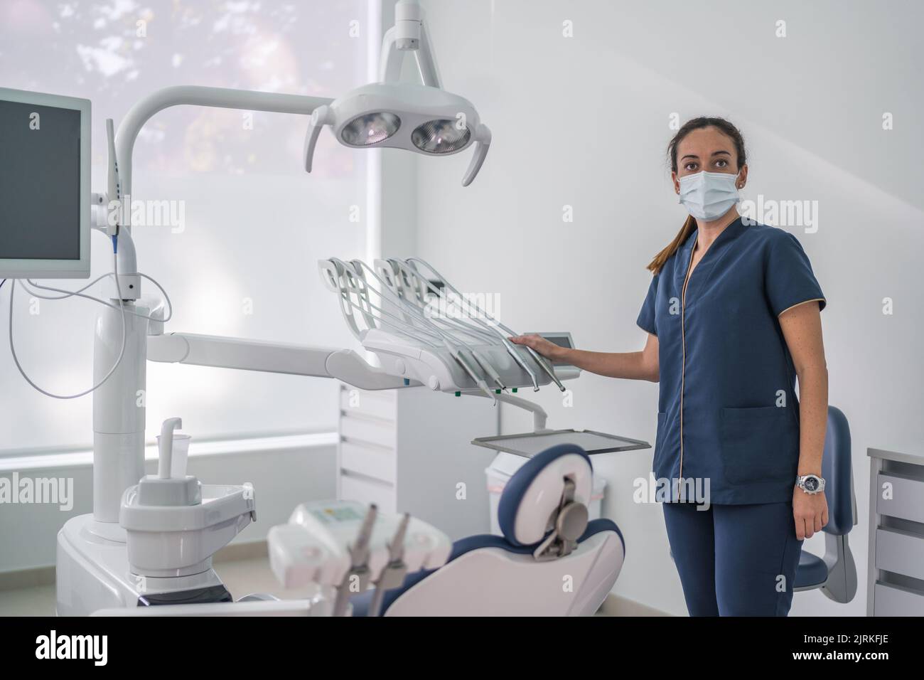 Side view of woman in medical uniform and mask adjusting tools settings ...