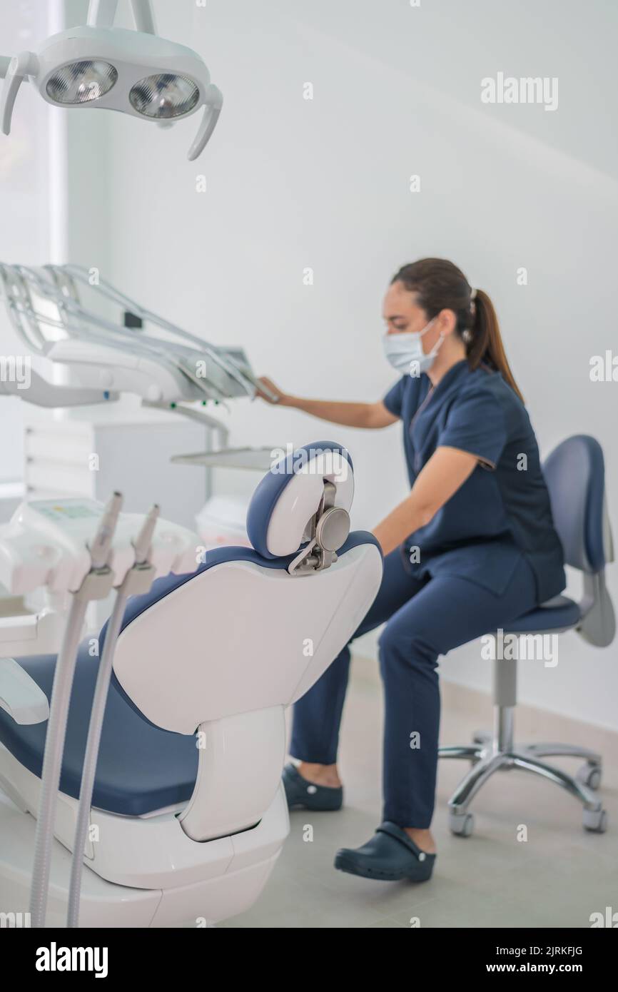 Side view of woman in medical uniform and mask adjusting tools settings ...