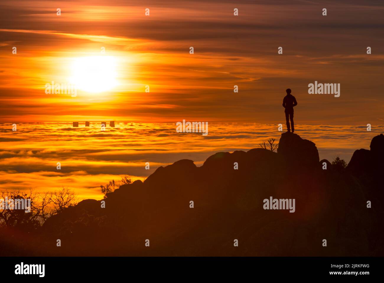 Back view of silhouette of male tourist standing on top of rock and ...