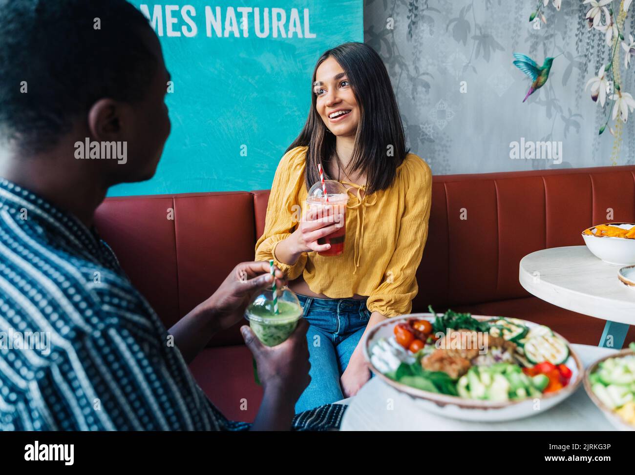 Content young female with glass of smoothie talking to crop ethnic ...
