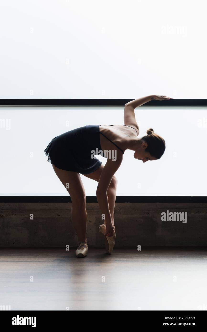 Young woman dancer bending down on dance studio floor and putting on ...