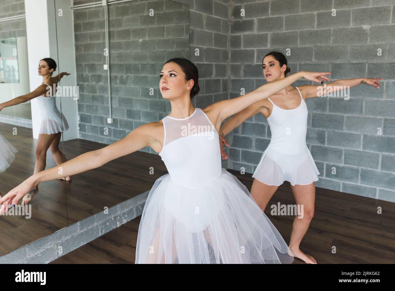 Two elegant young ballerinas dancing in synchrony next to a mirror at a ...