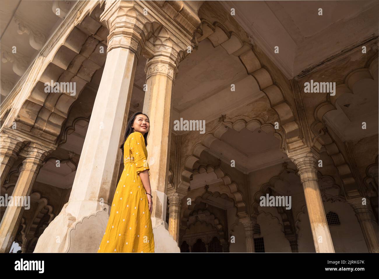 From below ethnic asian woman in yellow dress looking away while ...