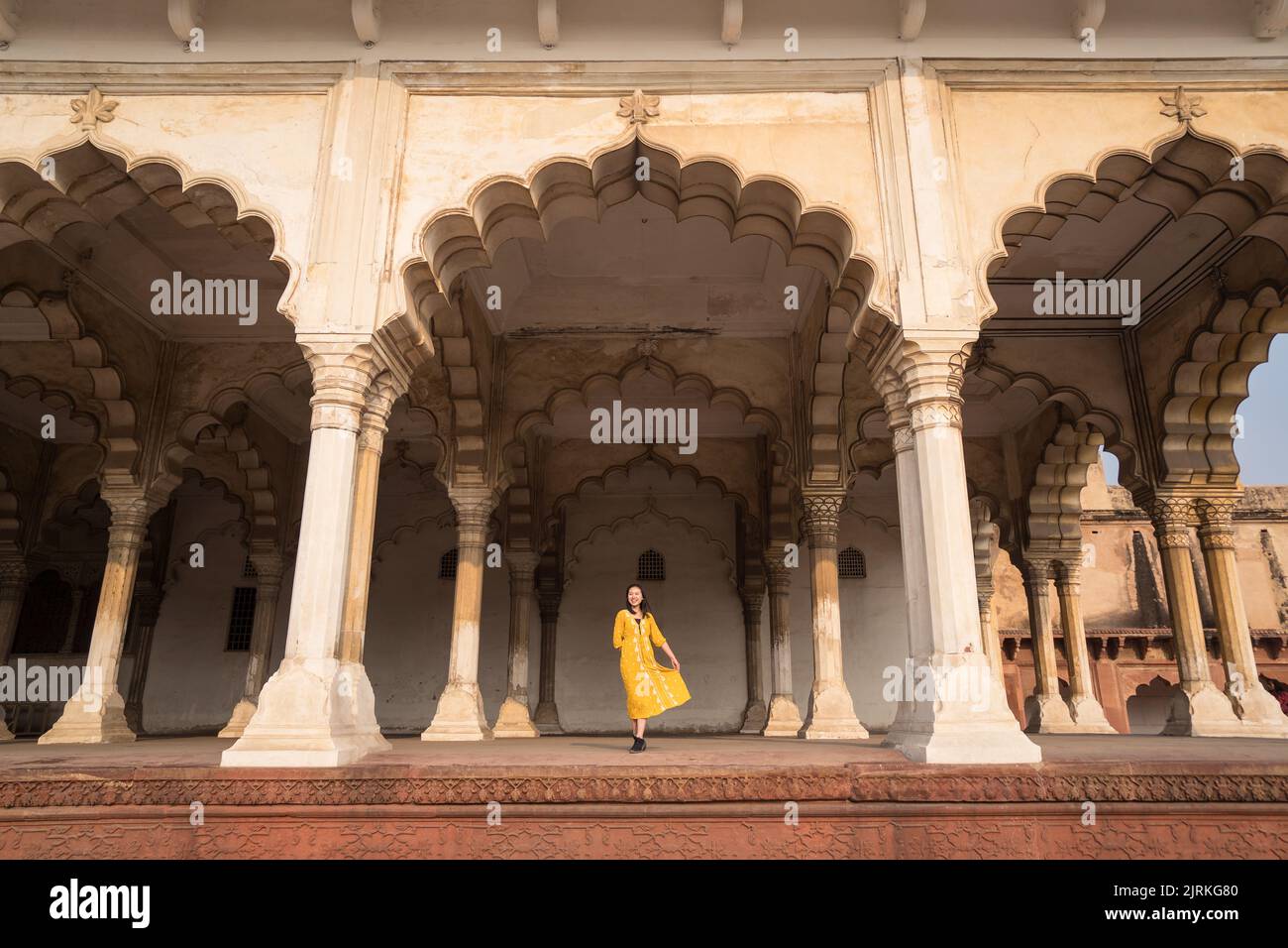 Happy ethnic woman in yellow dress looking away while standing amidst ...