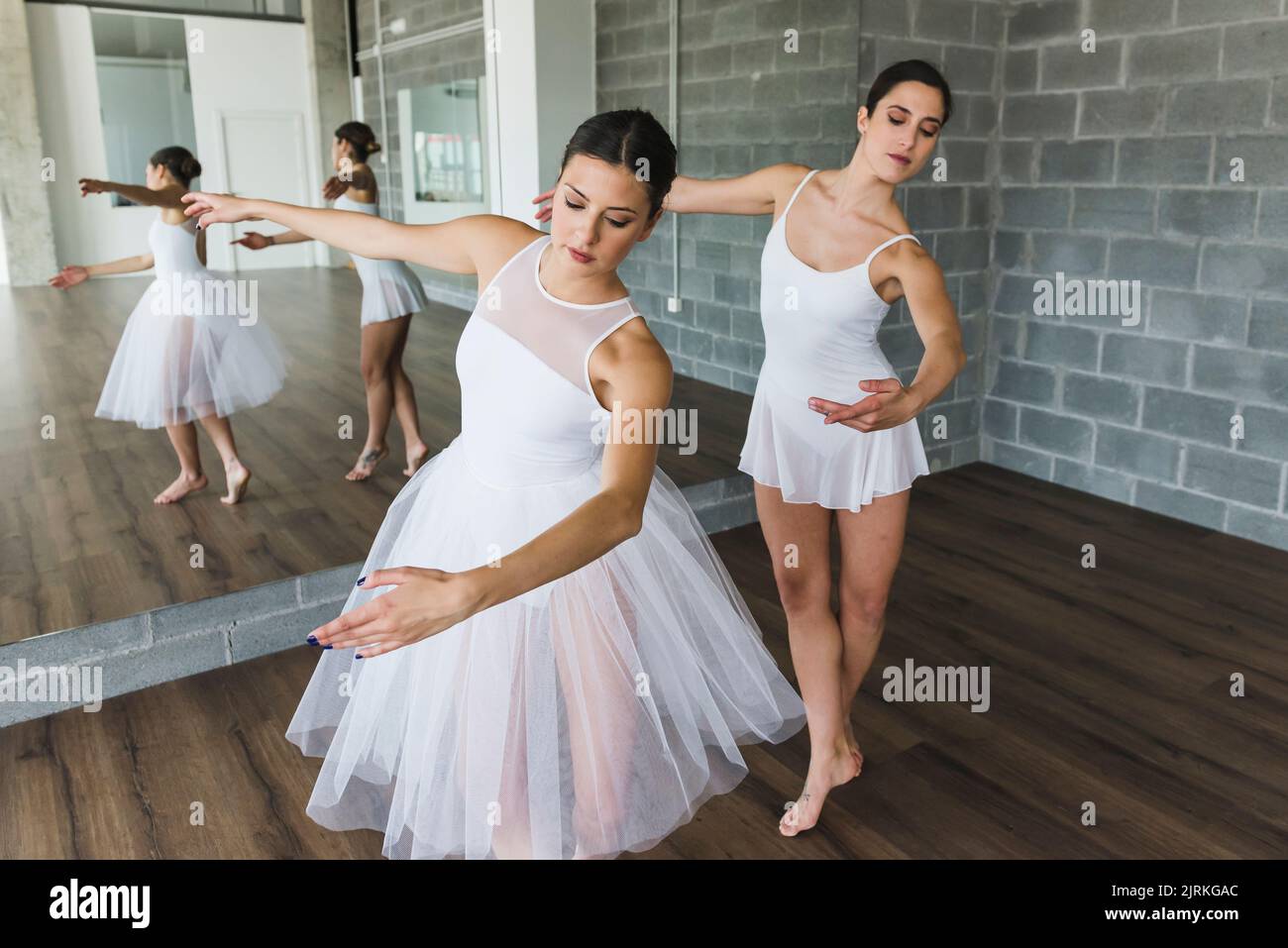 Two elegant young ballerinas dancing in synchrony next to a mirror at a ...