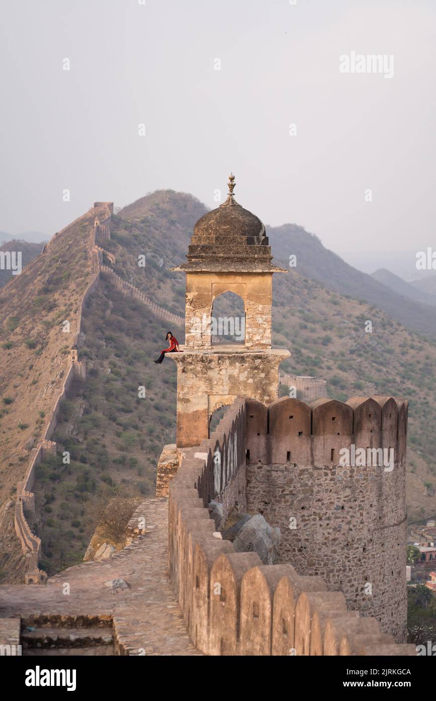 Woman sitting in arch of old tower against mountain ridge and walls ...