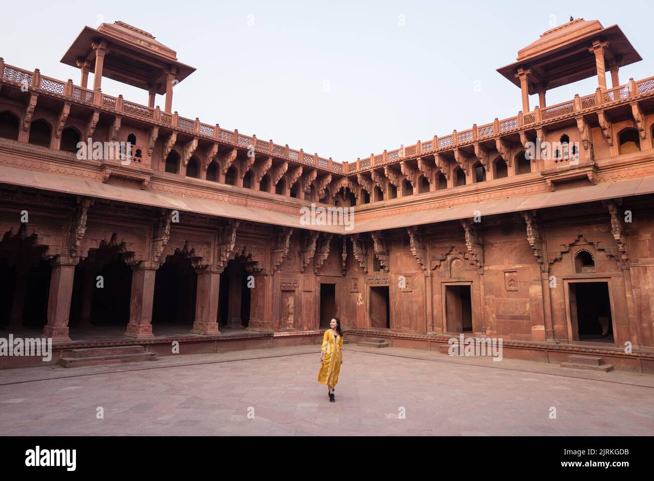 Ethnic Asian woman looking away in yellow dress standing in aged arched ...