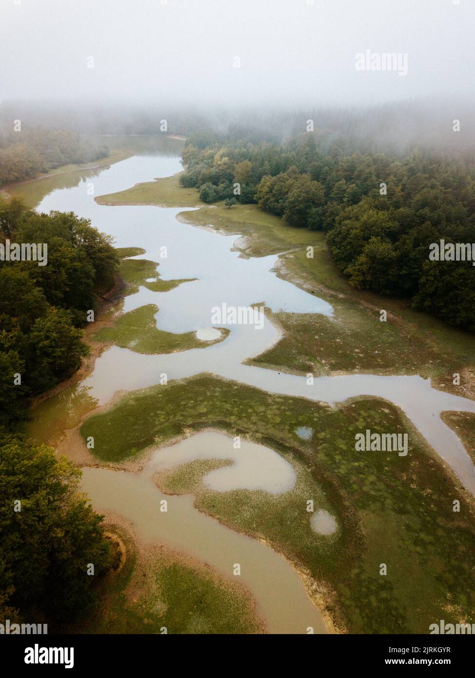 From above view of sinuous river running across misty forest at fall in ...