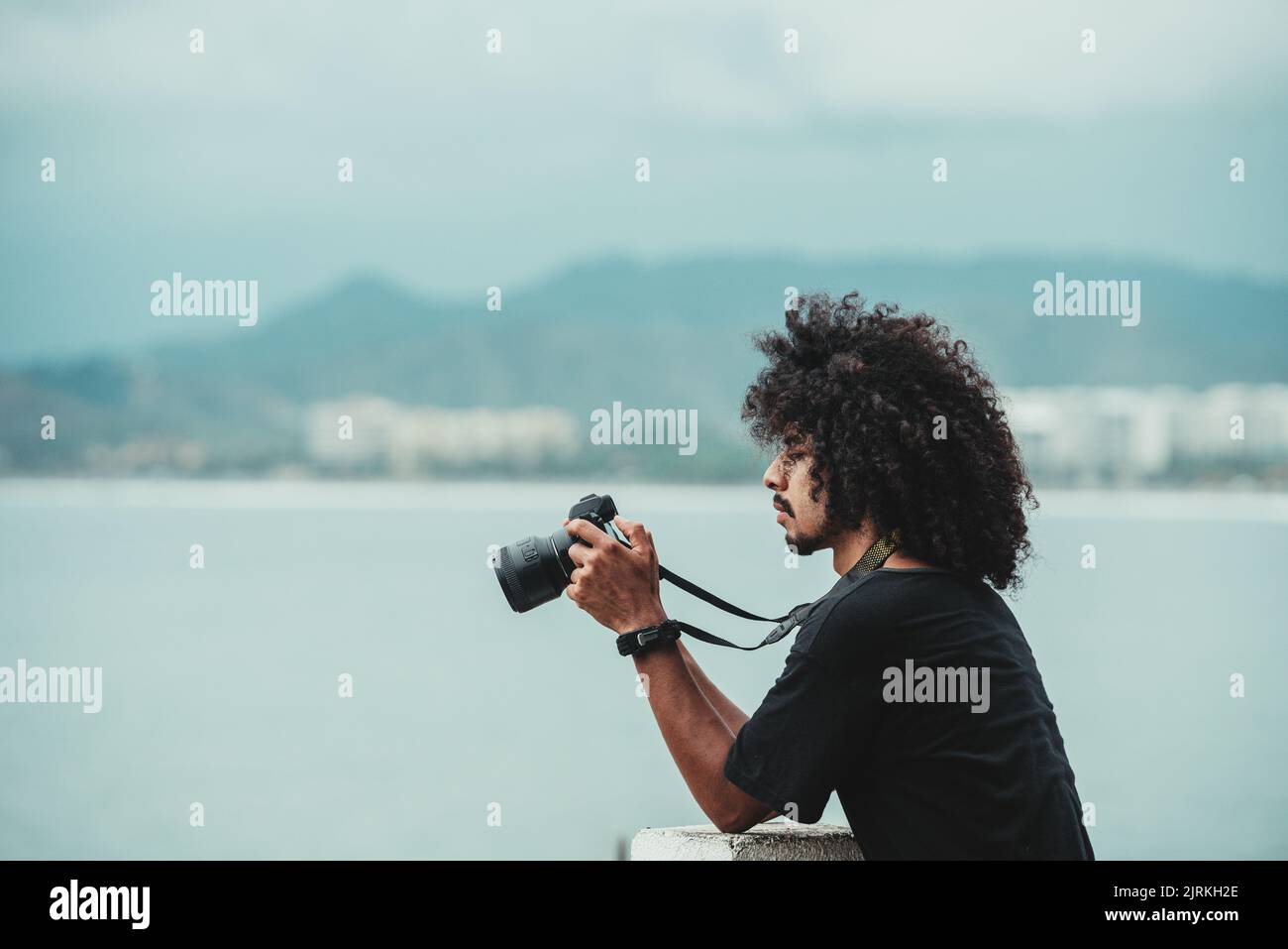 Side view of ethnic male with Afro hairstyle taking photo of ocean on ...