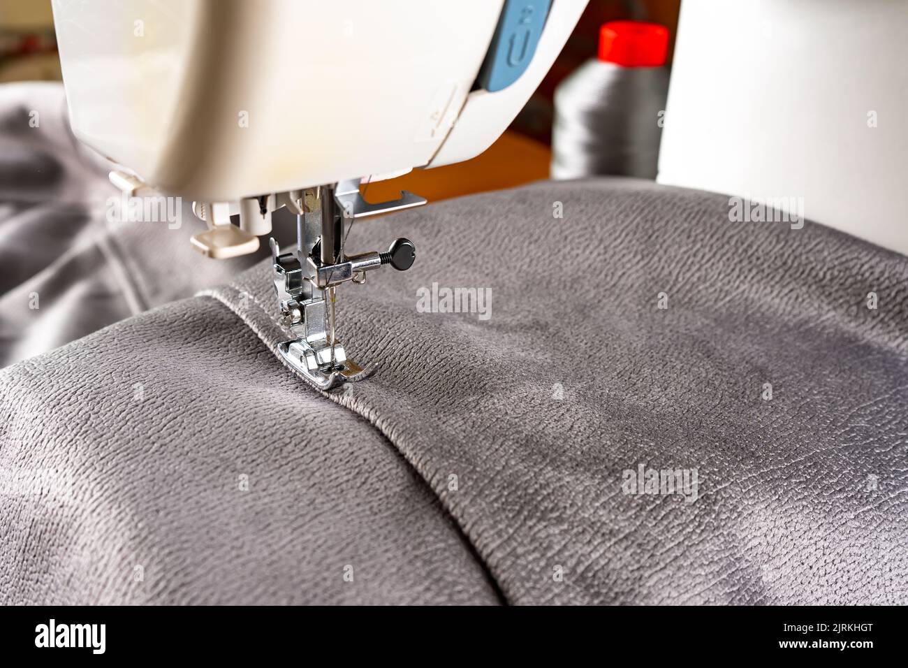 Modern sewing machine presser foot with gray fabric and thread, closeup ...