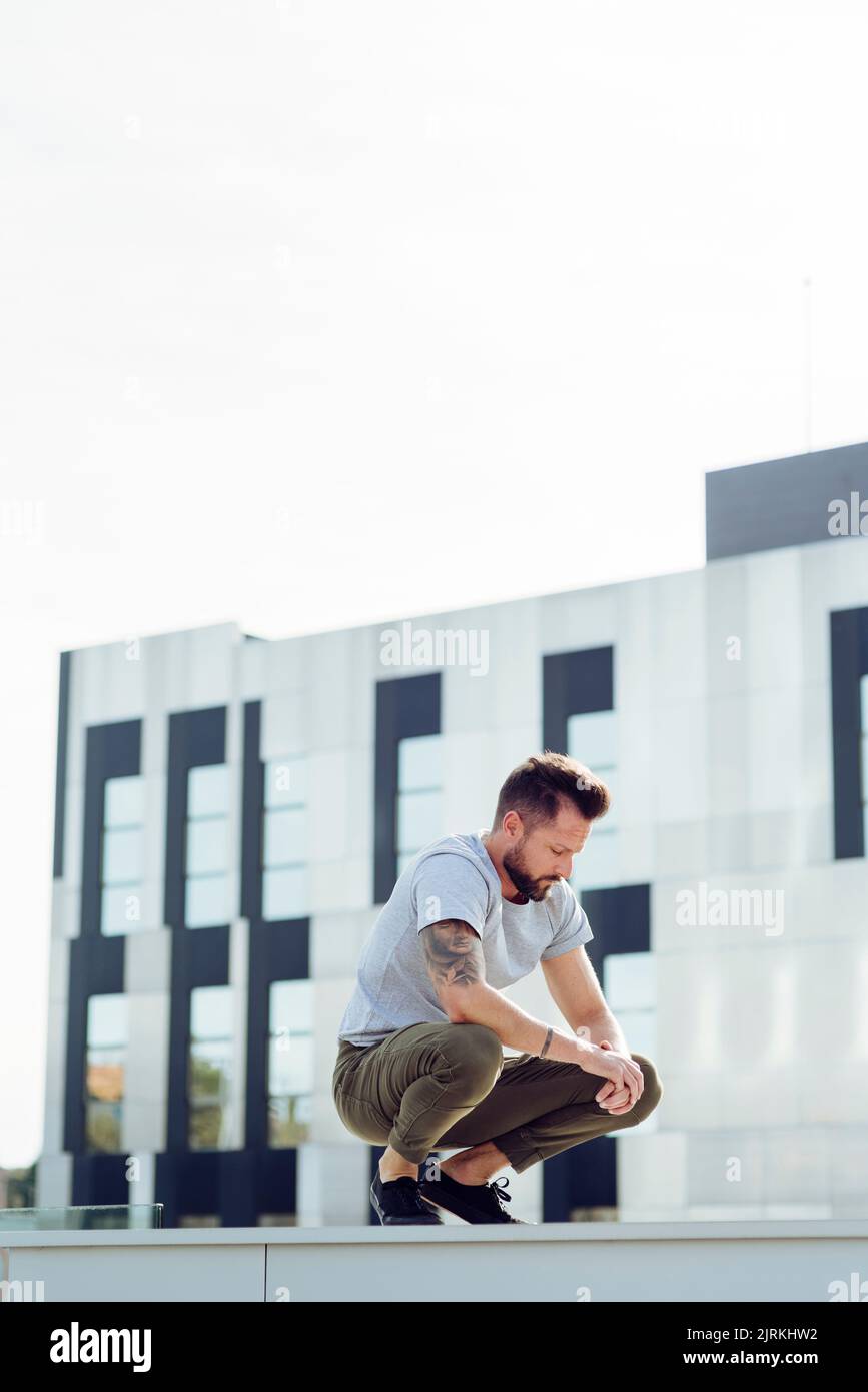 Athletic man resting crouching down after doing parkour balance ...