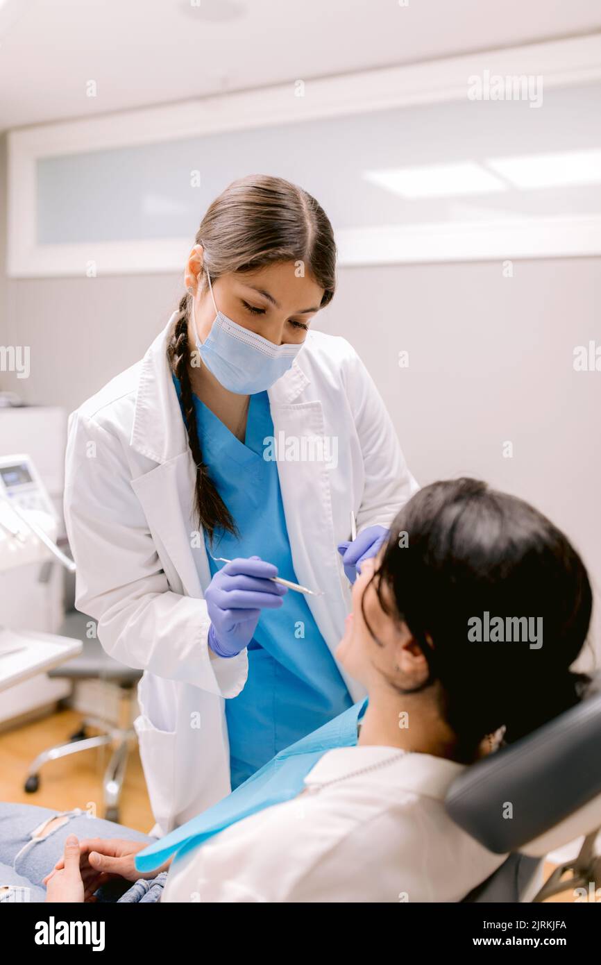 Female stomatologist in disposable mask and uniform checking up teeth ...