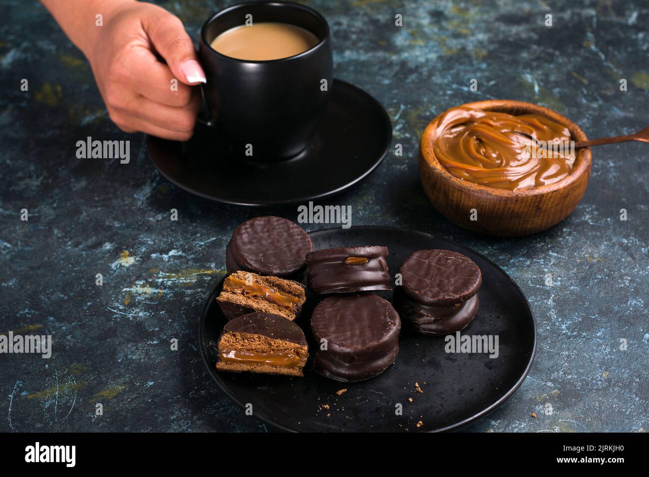 Chocolate alfajores with dulce de leche placed on black plate against ...