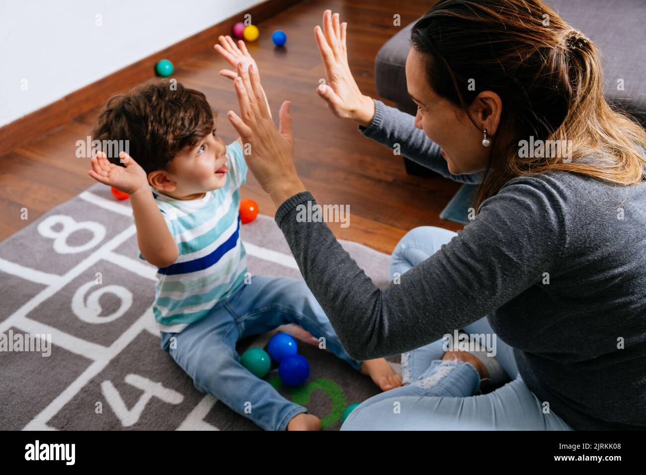 From above funny boy clapping hands with mother while sitting on floor ...