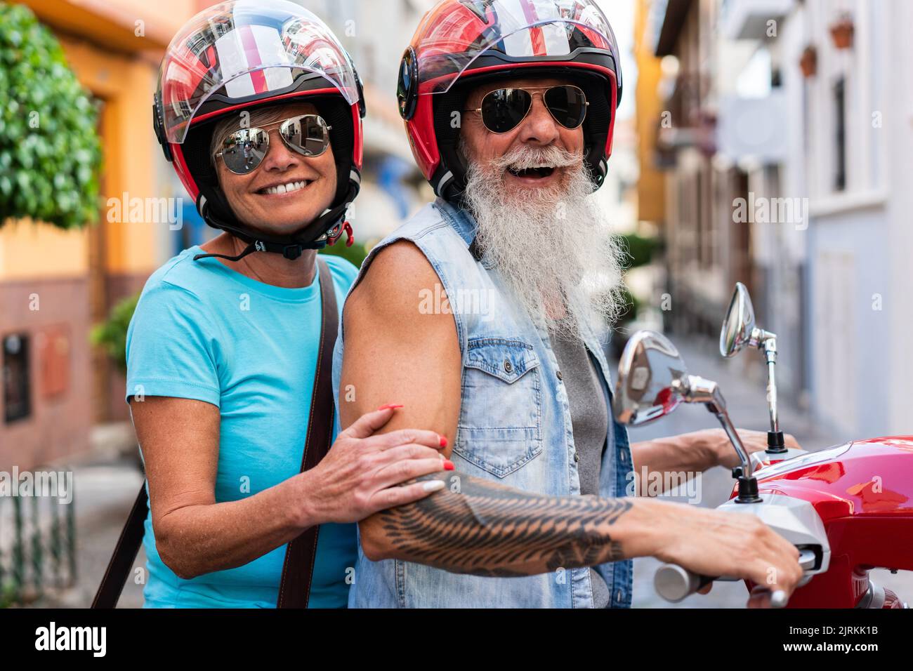 Side view of a modern senior couple with helmets riding a red ...