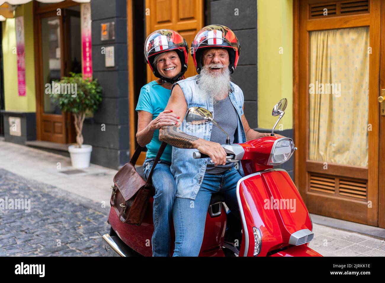 Side view of a modern senior couple with helmets riding a red ...