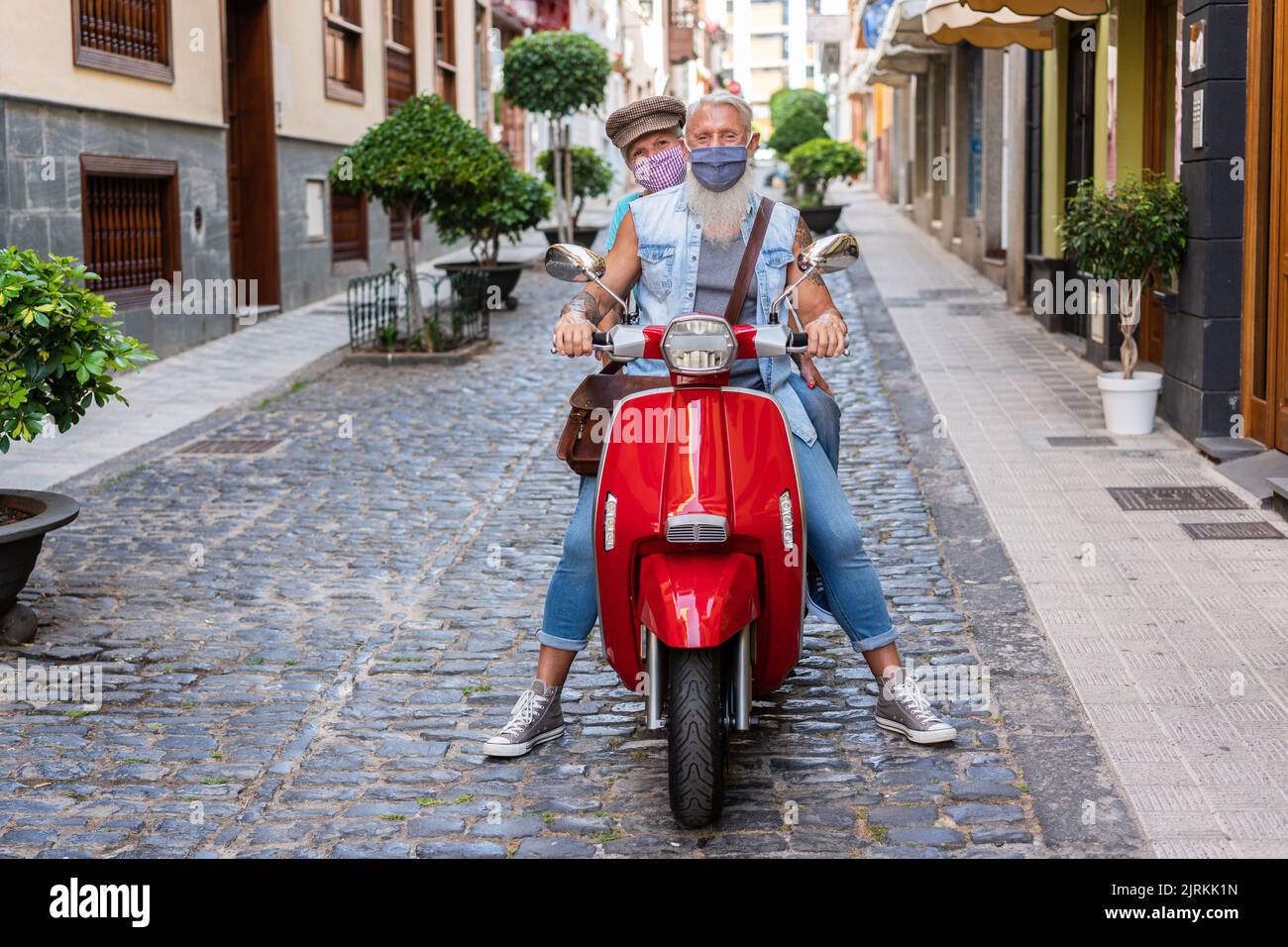 Front view of a modern senior couple with masks riding a motorcycle ...