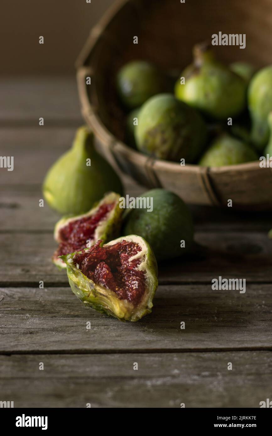 Closeup shot of basket with green figs and split fruit with red flesh ...