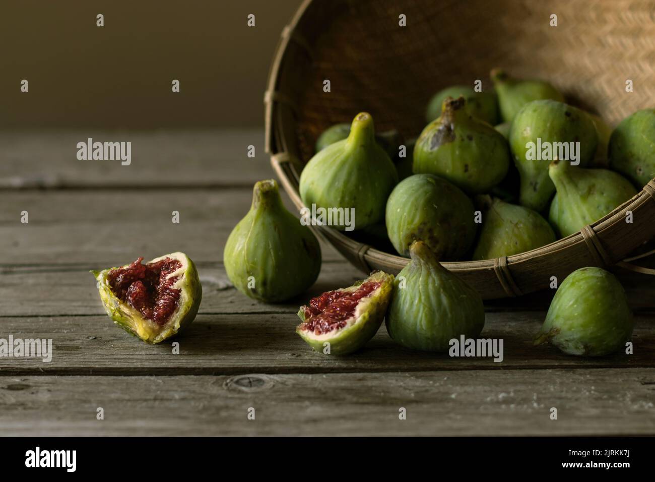 Closeup shot of basket with green figs and split fruit with red flesh ...