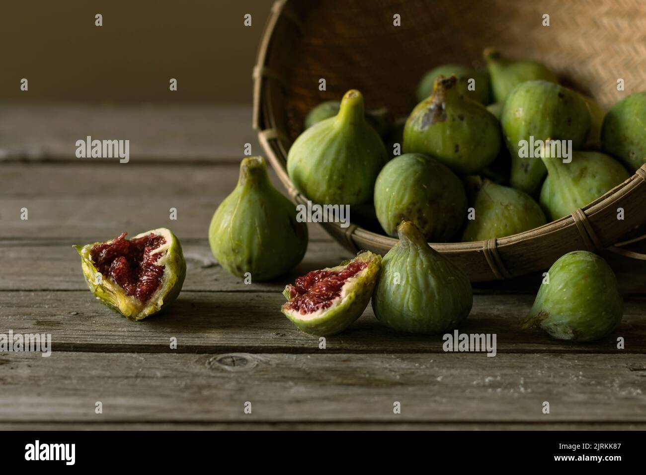 Closeup shot of basket with green figs and split fruit with red flesh ...