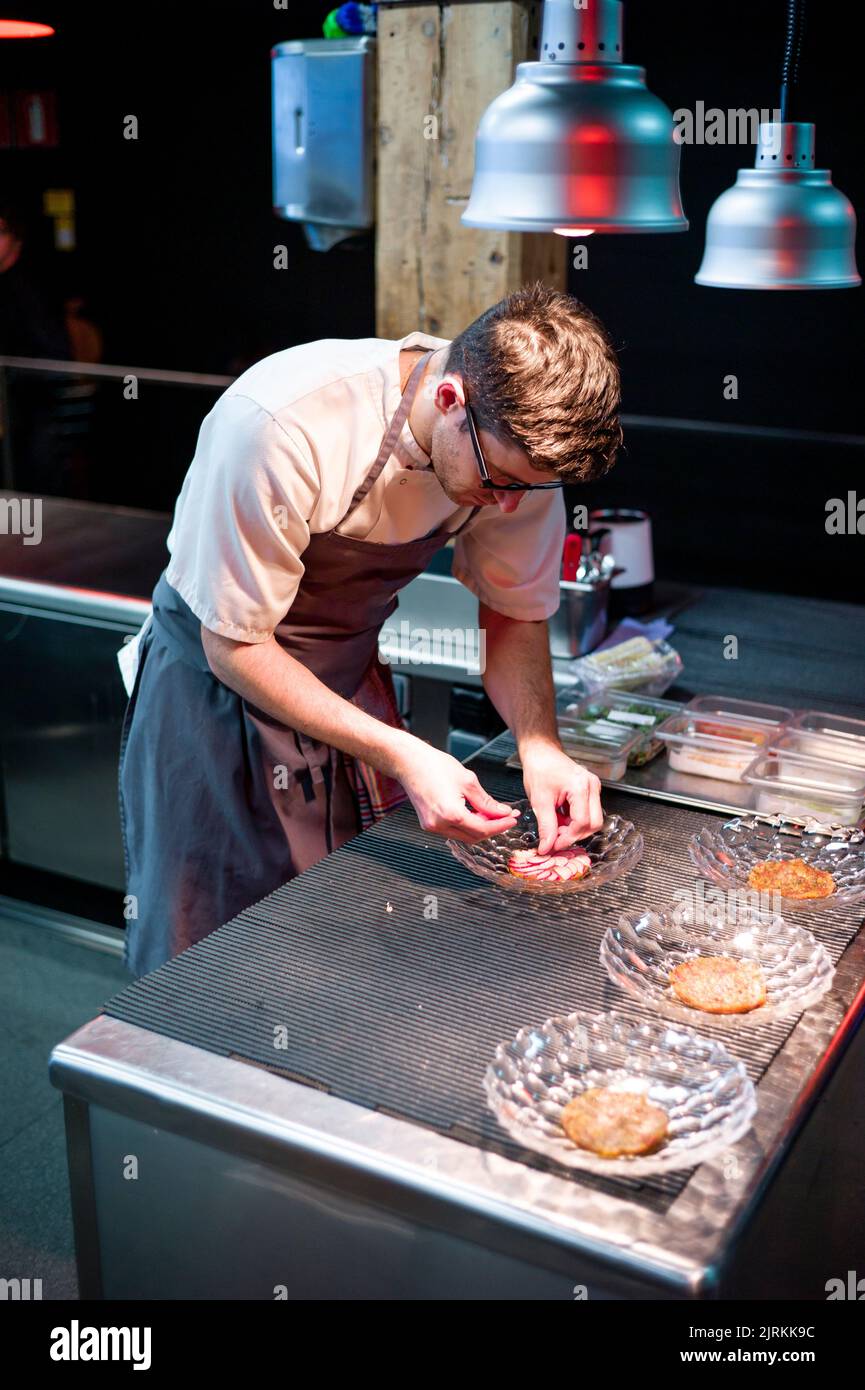 Young serious chef man in cooking apron serving meal in dishes on ...
