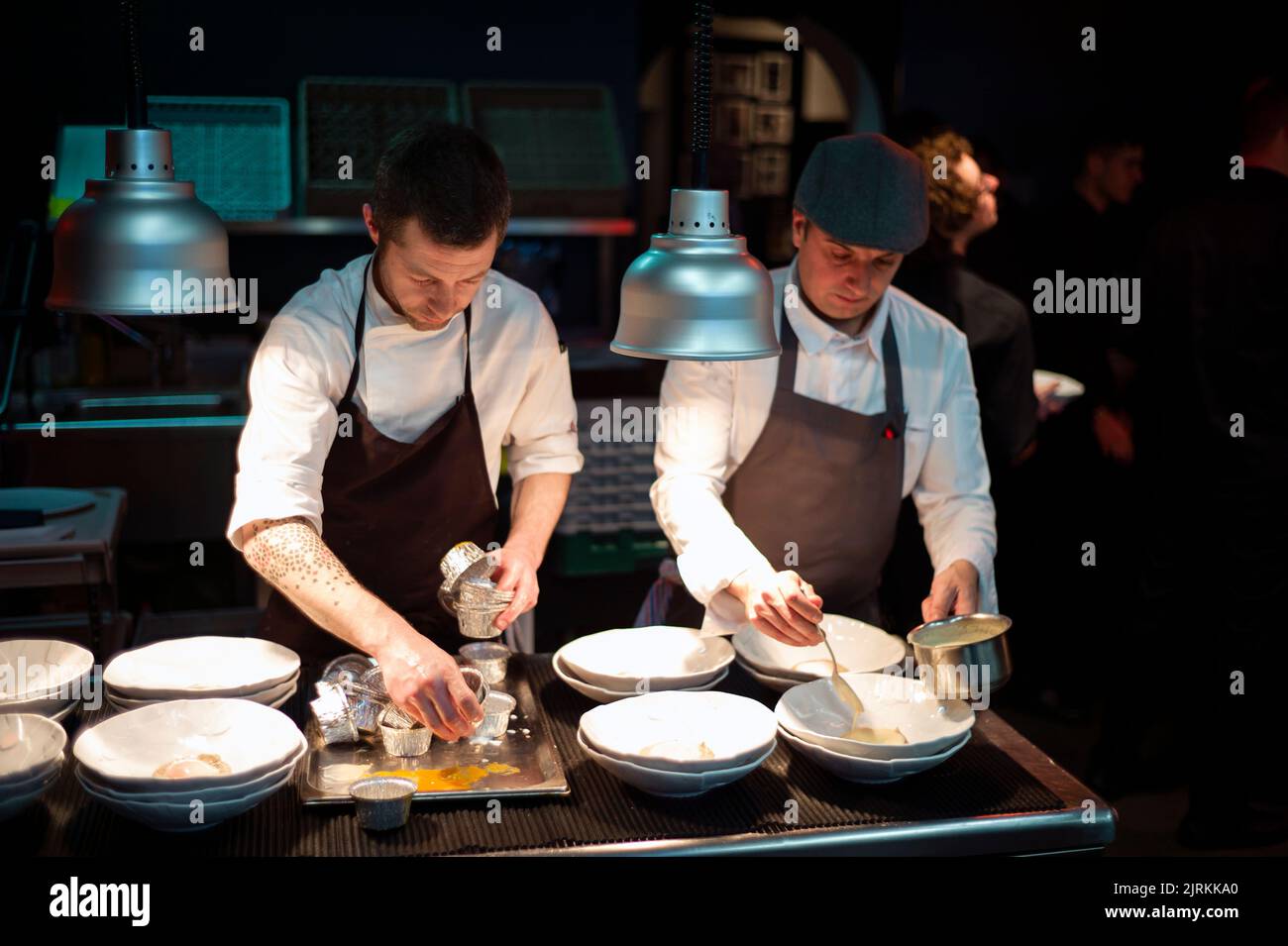 Young cooks men in aprons carefully serving meal in white ceramic ...