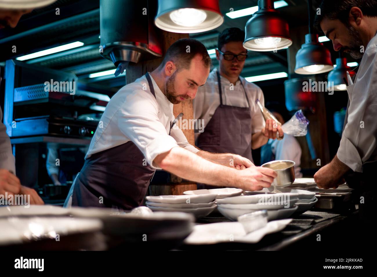 Young cooks men in aprons carefully serving meal in white ceramic ...