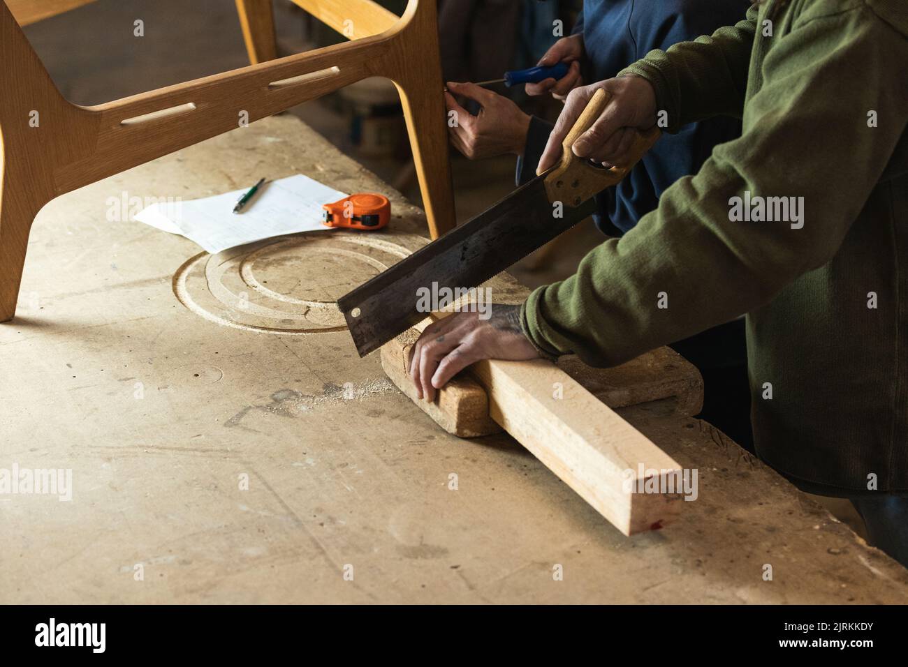 From above unrecognizable carpenters cutting with saw and measuring ...