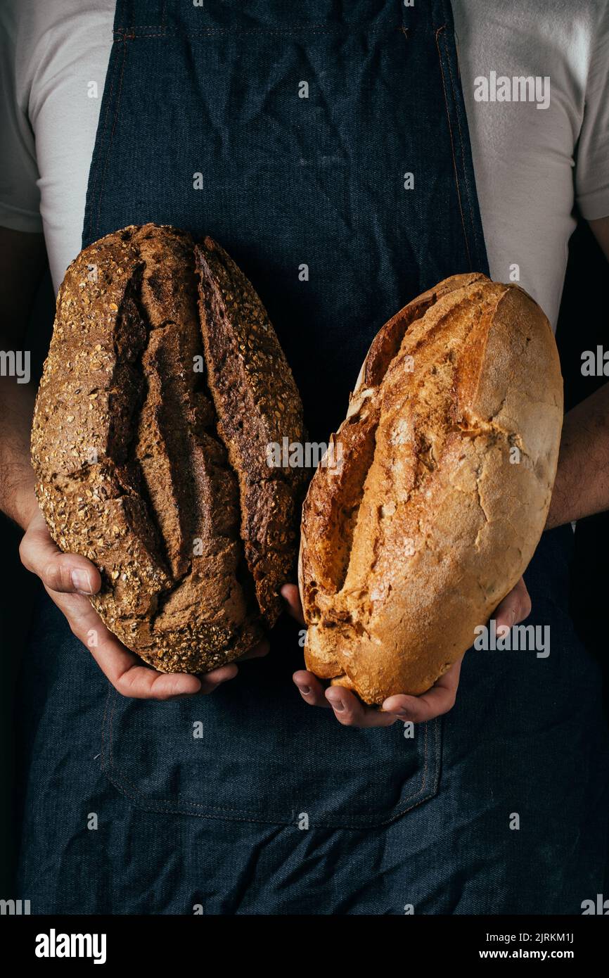 Crop unrecognizable male baker in apron demonstrating loaf of fresh ...